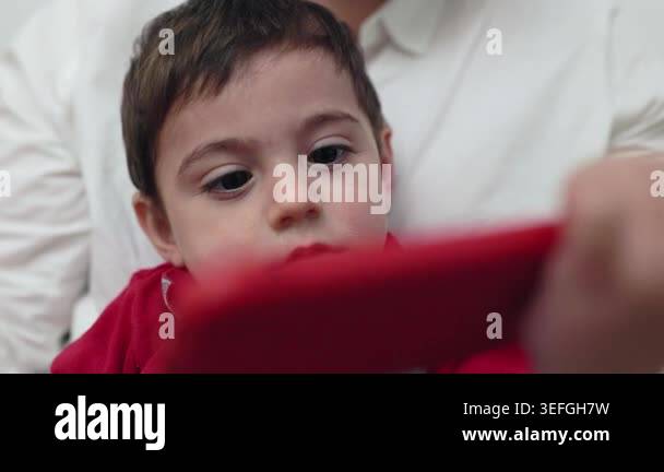 Cute little boy sitting on his mothers lap while watching cartoons on a ...