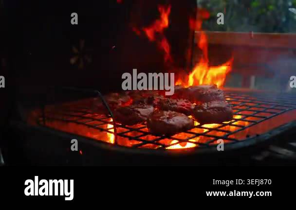 Beef burgers grilling over open flames on barbecue grill. Multiple meat ...