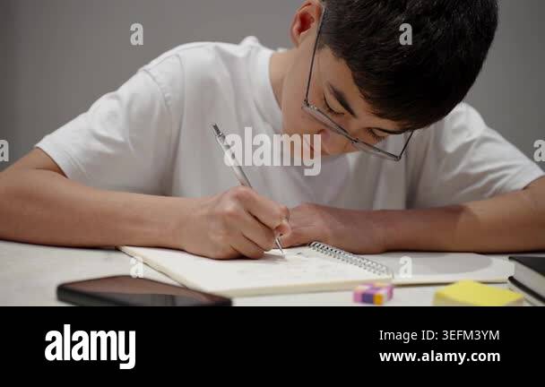 Concentrated pupil writing notes in notebook during study session at ...