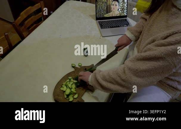 Woman slicing fresh cucumbers on cutting board while following online ...
