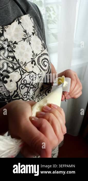 Close-up of hands skillfully piping a delicate buttercream rose flower ...