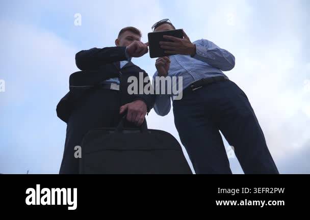Two young businessmen talking and using tablet pc in city. Handsome ...