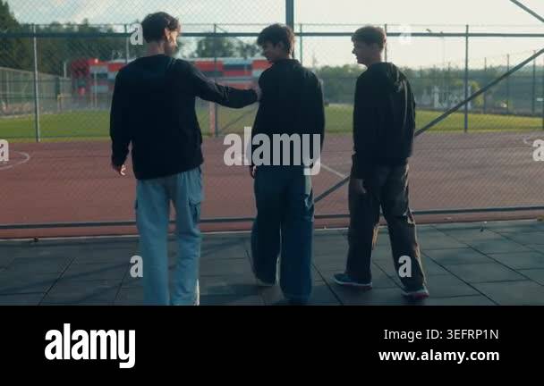 Right after class, three teen boys hang out beside the sports field ...