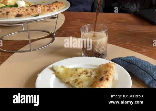 Cola is poured into a glass beside a freshly served cheese pizza. The ...