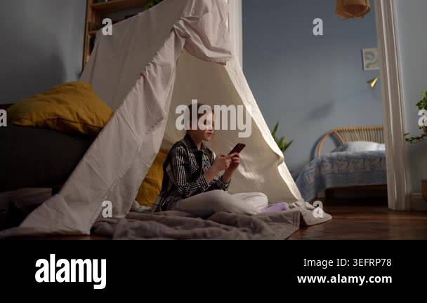 White girl sitting blanket fort texting, soft ambient light, phone glow ...