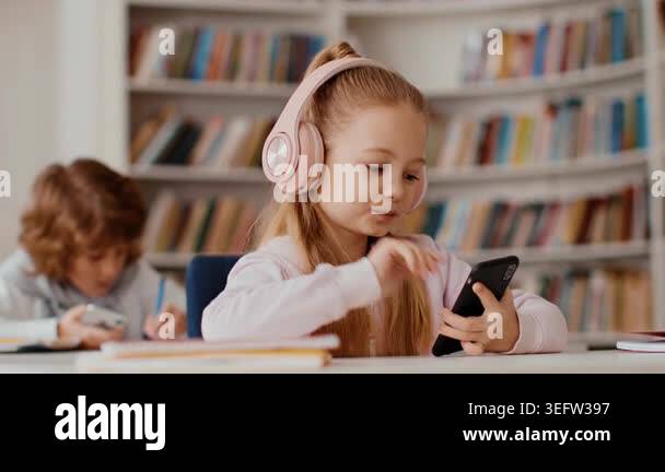 A girl with light skin is sitting at a table in a library, wearing ...
