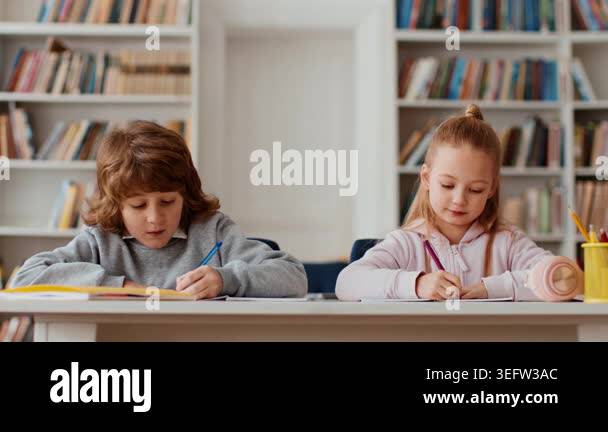 Two children are sitting at a table in a bright classroom with ...