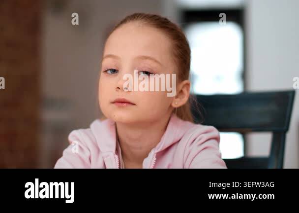 A girl with light skin is sitting at a table with a big smile. She ...