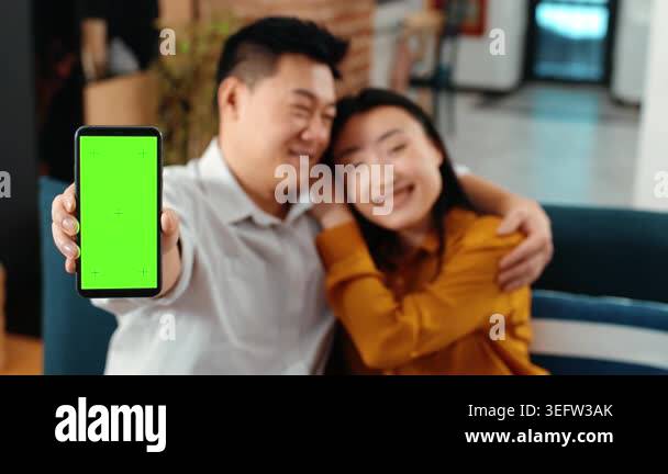 An Asian man and woman smile while sitting together in a modern living ...