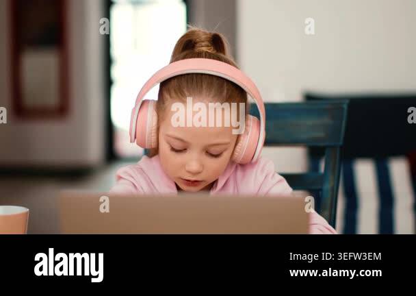 A girl with light skin is focused on her laptop while wearing pink ...