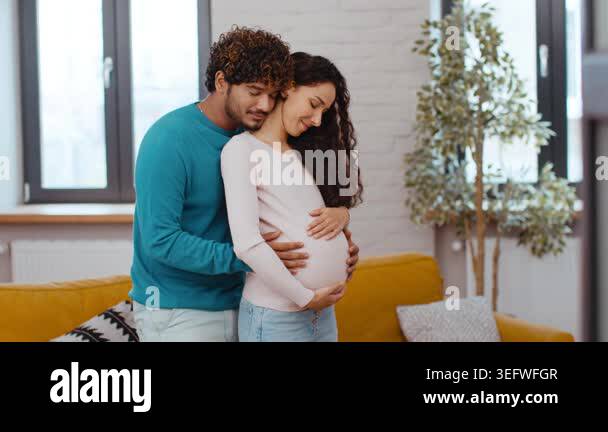 A man with curly hair stands behind a woman with long curly hair. She ...