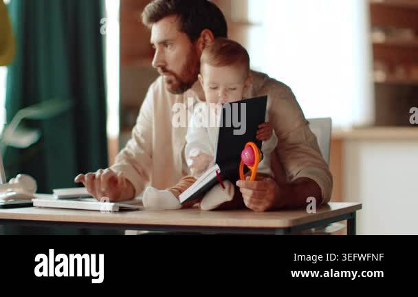 A man with light skin is seated at a desk working on a computer while a ...