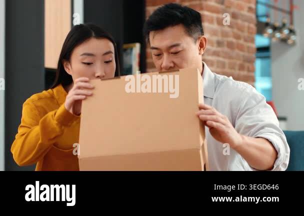 A man and a woman are smiling and looking at a cardboard box they are ...