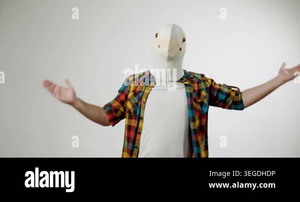 A man wearing a bird mask turns to the camera and stretches his arms ...