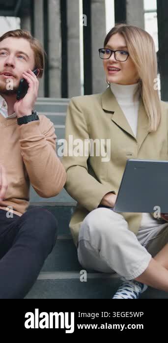 Attractive man and woman sitting on stairs in urban city center working ...