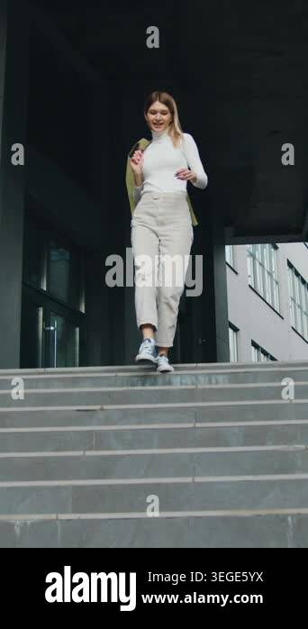 Active and confident beautiful young woman goes down the stairs smiling ...