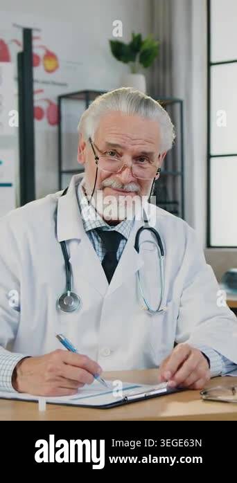 Portrait of happy mature male doctor holding clipboard while sitting ...