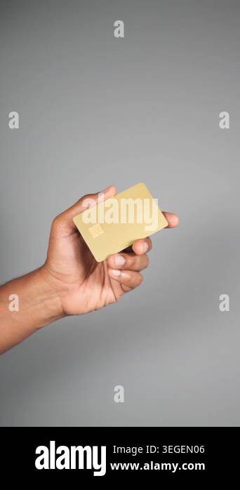 A person holds a gold credit card in their hand against a grey ...
