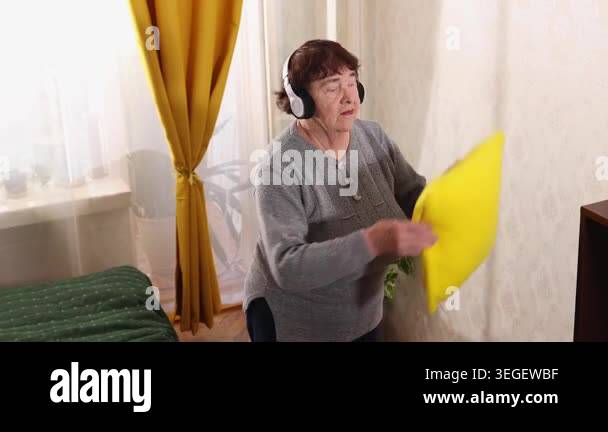 Older Caucasian woman dancing in apartment with headphones and smile ...
