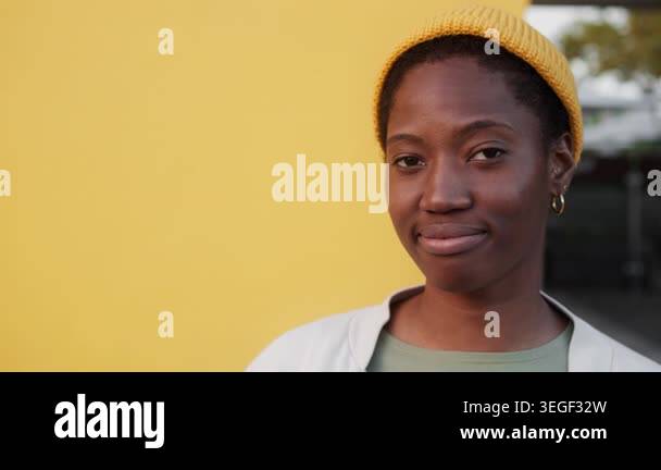 Smiling Black young woman near bright yellow wall during daytime in ...