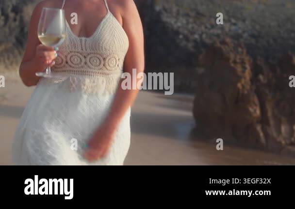Smiling young woman in white dress walking on sandy beach near ocean ...