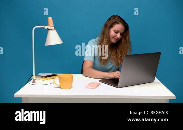 Pretty young student working on her laptop and smiling at her desk. She ...