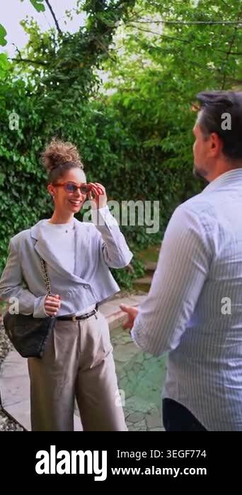 Stylish young woman smiling and talking with a man in a lush green ...