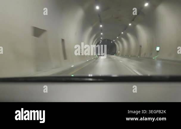 Point of view shot exiting a modern lighted tunnel onto a dark, wet ...