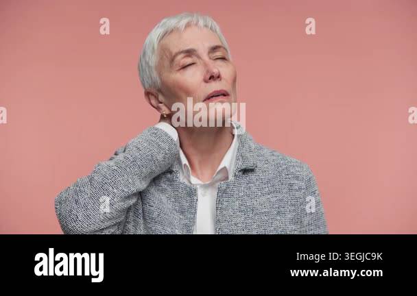 Older woman with short gray hair holds her neck with closed eyes ...