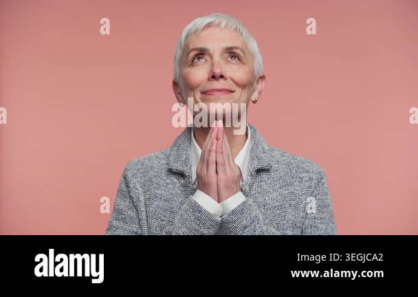 Older woman with short gray hair clasps her hands and looks upward ...