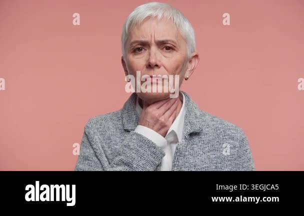 Unwell senior woman touches her neck with a worried expression, showing ...