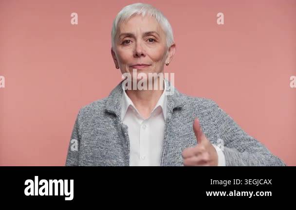 Older woman with short gray hair smiles gently while giving a thumbs up ...