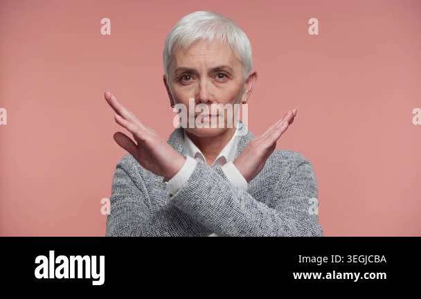 Older woman with short gray hair crosses her arms in a firm stop ...