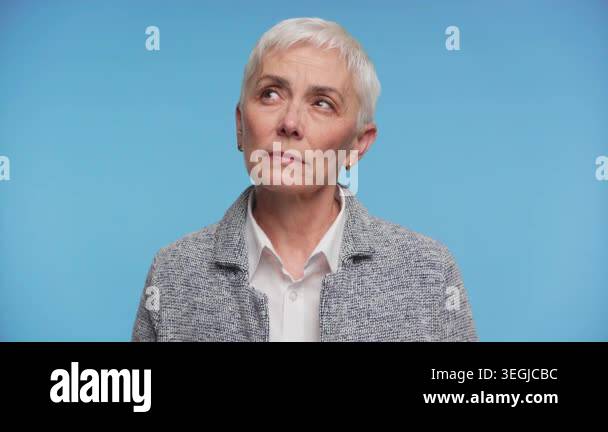 Mature woman with short gray hair looks upward thoughtfully, expressing ...
