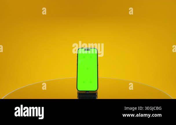 Smartphone with green screen stands centered on a reflective surface ...