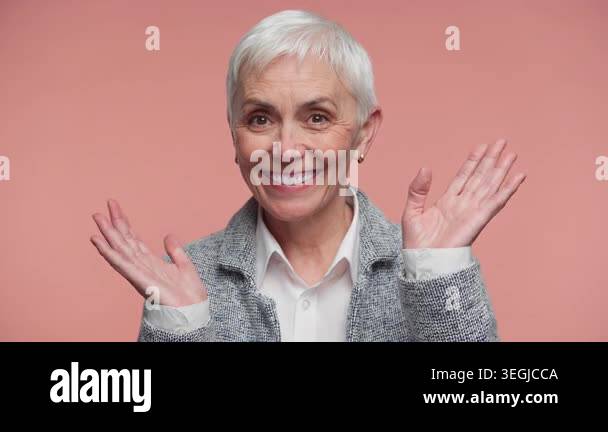 Older woman with short gray hair smiles warmly and raises both hands in ...