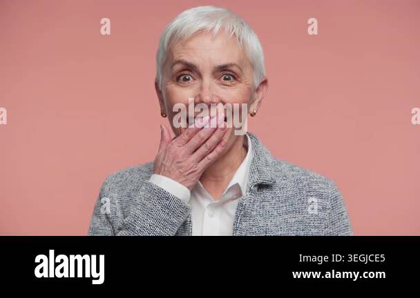 Older woman with short gray hair covers her mouth in happy surprise ...