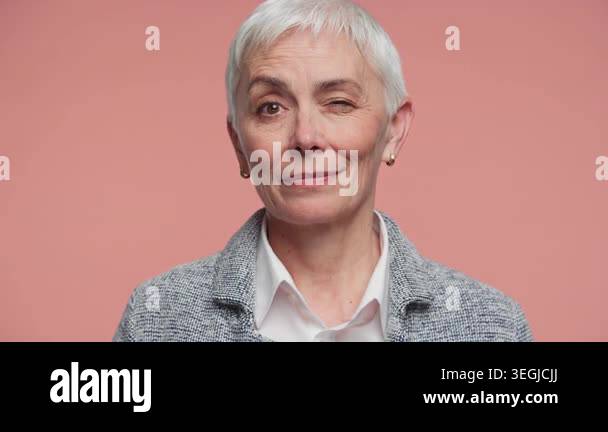 Older woman with short gray hair winks playfully with a calm smile ...