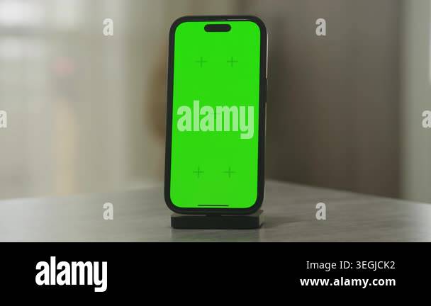Modern smartphone standing on a table with a bright green screen for ...