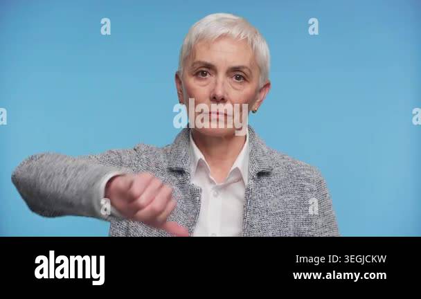 Mature woman with short gray hair gives a thumbs down sign with a ...