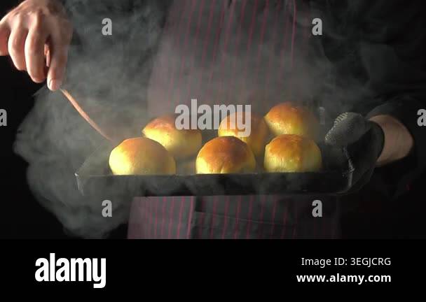 Chef in a black apron presents a tray of golden rolls, steam rising ...