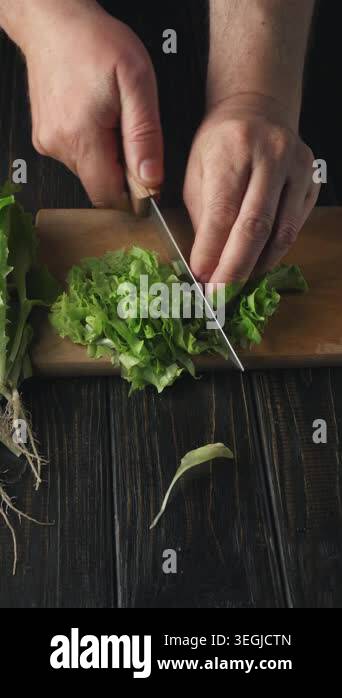 Hands of a person in a kitchen slicing fresh green lettuce on a wooden ...