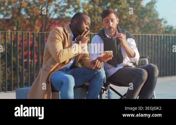 Black man and white man sharing smartphone on outdoor terrace, both ...