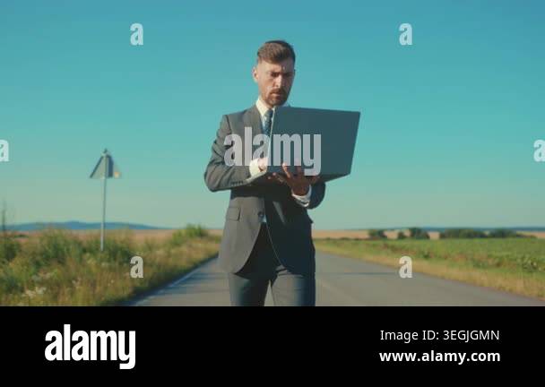 Caucasian man using laptop on open road, tailored suit, concentrated ...