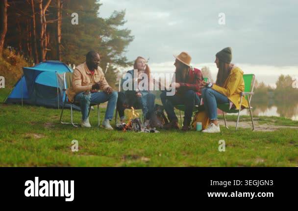 white and black friends camping lakeside by tent and bonfire ...