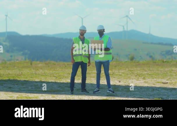 two engineers review wind project plans, sunny plateau with turbines on ...
