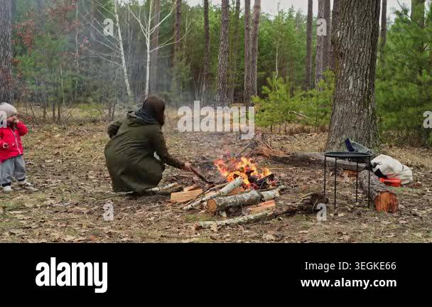 Woman digging soil with a shovel around a strong campfire in the forest ...