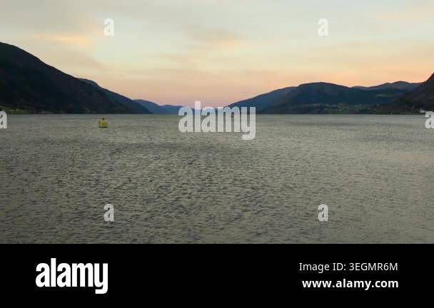 Wide cinematic view of a calm fjord at sunset with pastel sky and ...