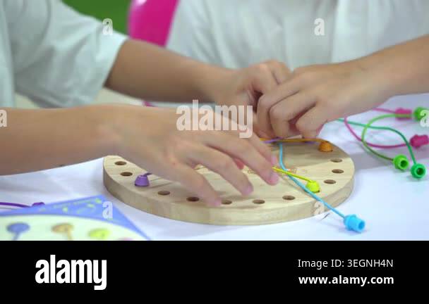 Close up of children's hands playing with a colorful wooden stringing ...