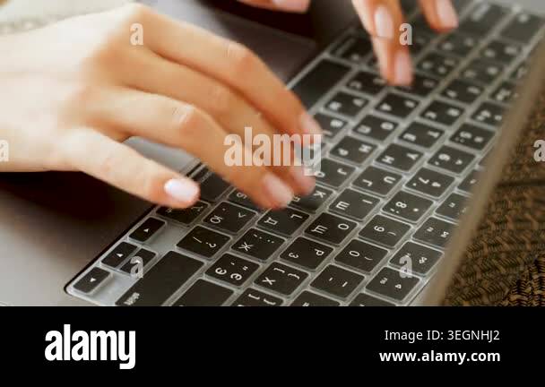 Hands type on a dark grey laptop keyboard. The keys display both ...